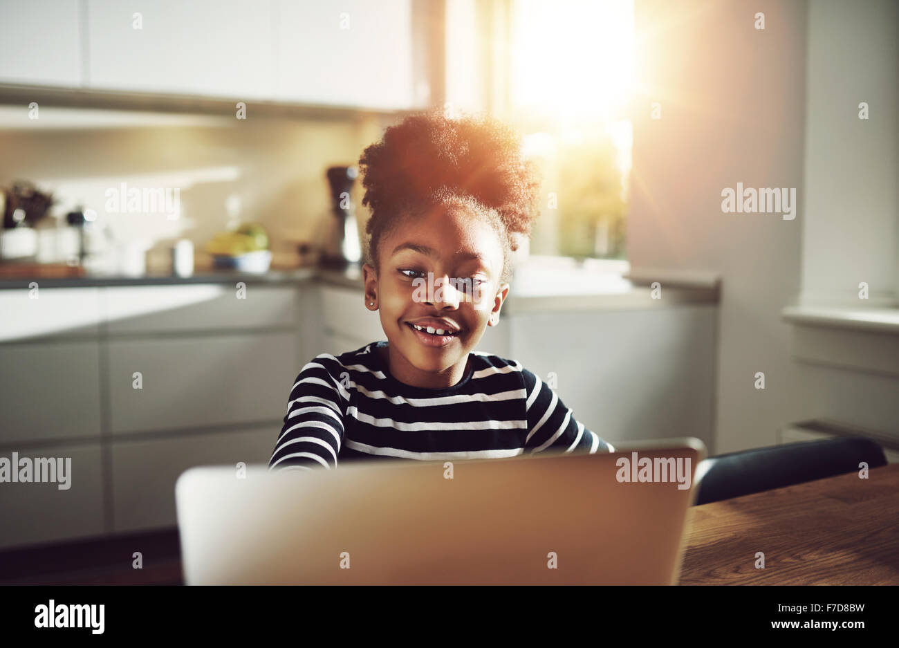 Cute young black girl playing on a laptop computer smiling happily as ...