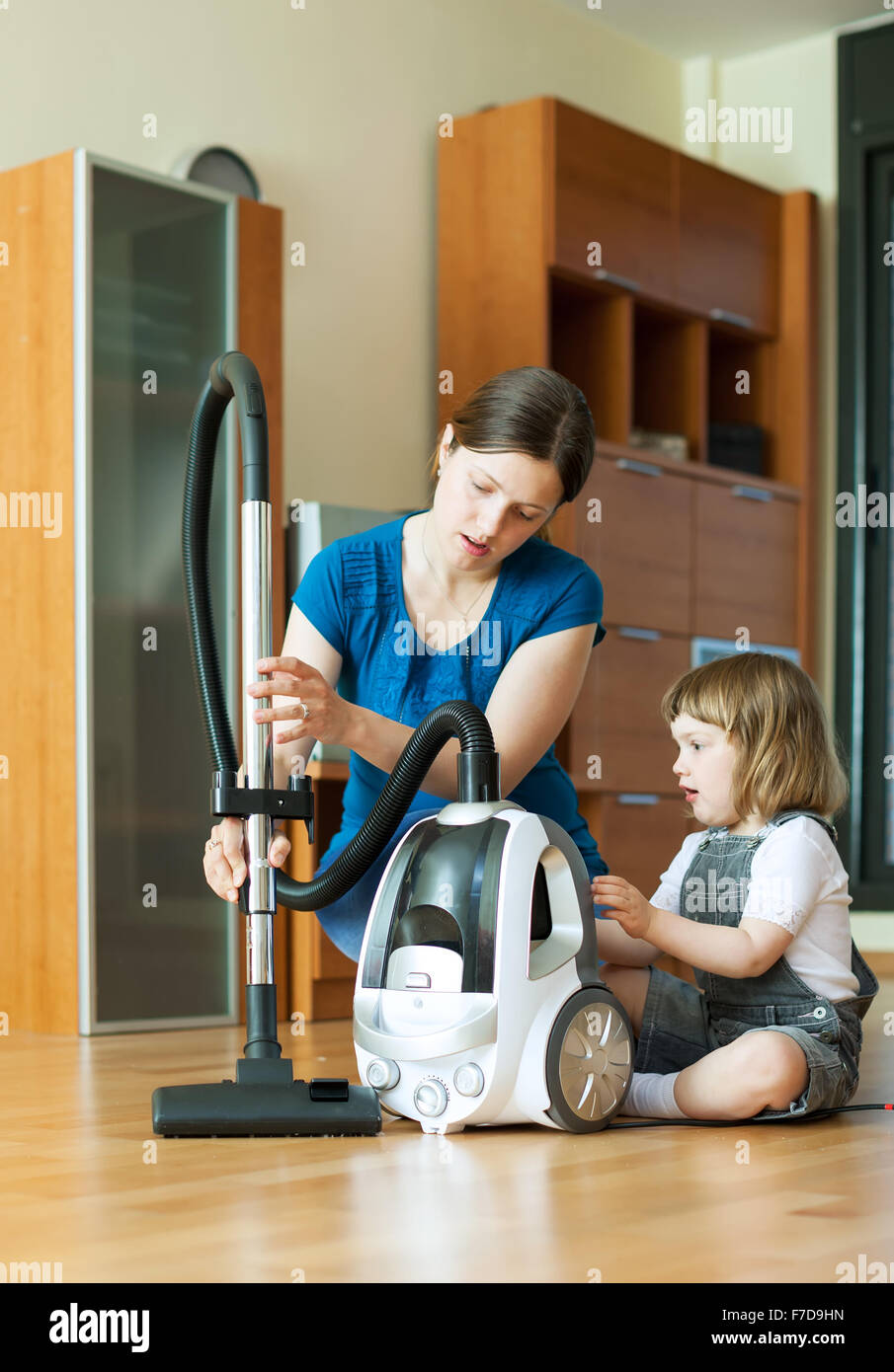 Woman teaches child to use the vacuum cleaner in living room Stock ...