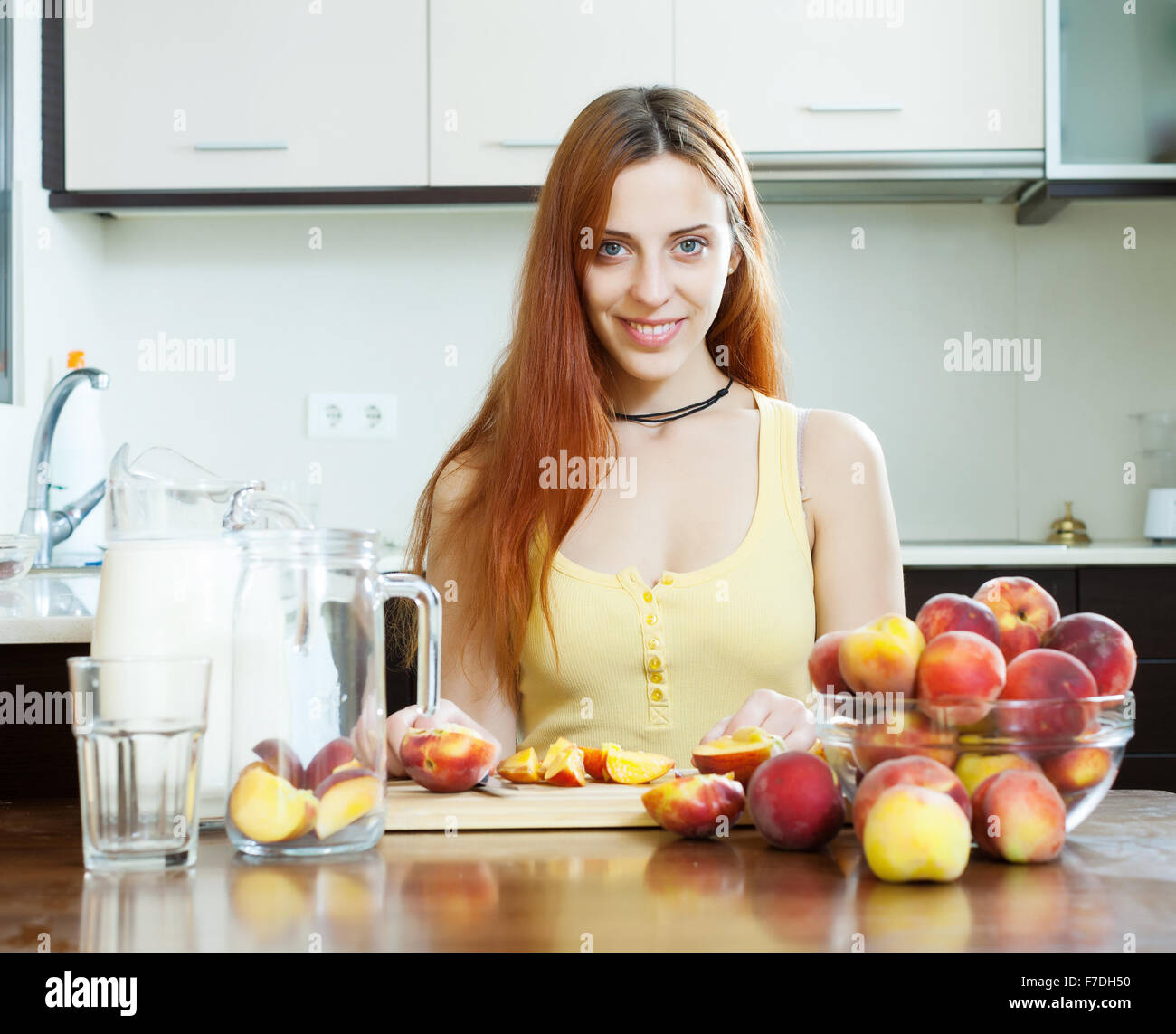 cheerful long-haired woman cooking beverages with peaches at home ...