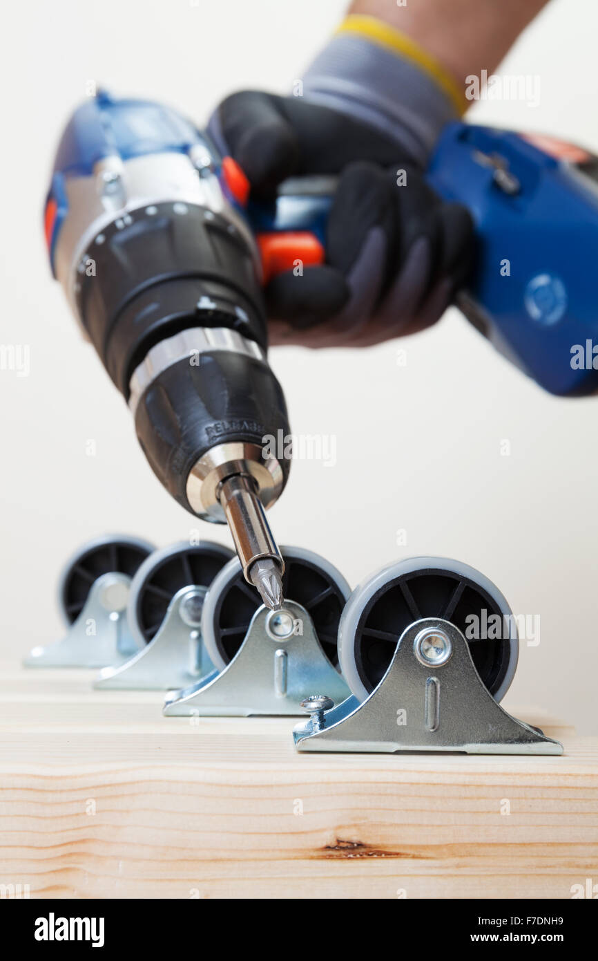 Assembling the furniture, fixing the wheels with cordless screwdriver ...