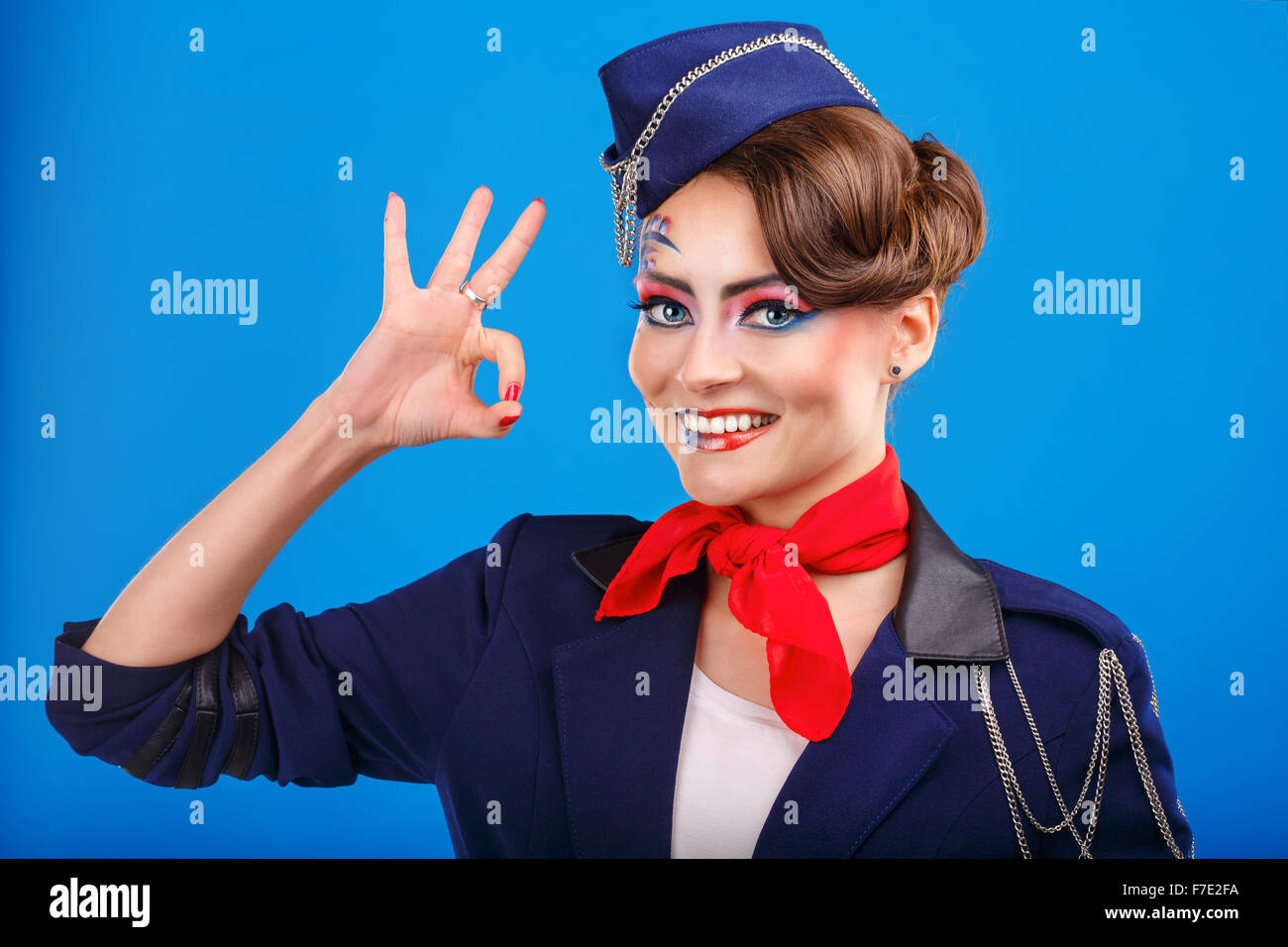 Stewardess with face art shows OK. Young attractive girl in a blue suit ...