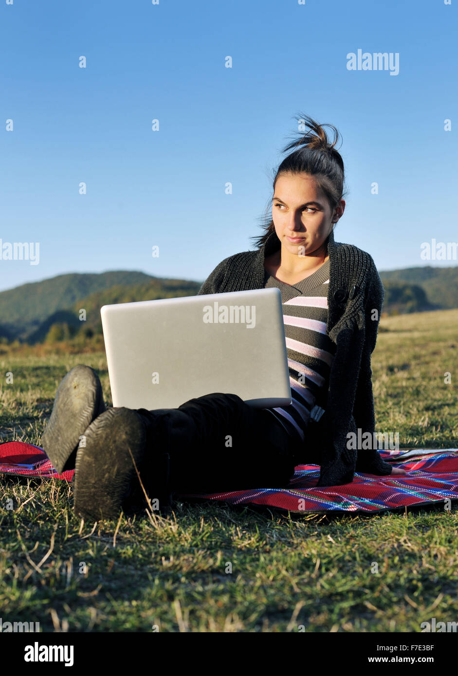 young teen woman work on laptop computer outdoor in nature with blue ...