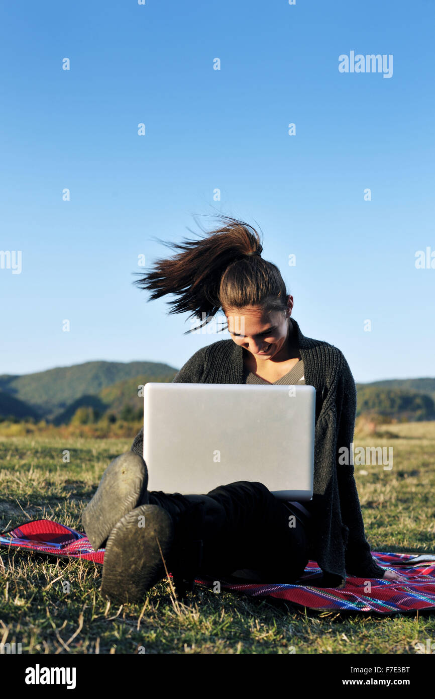 young teen woman work on laptop computer outdoor in nature with blue ...