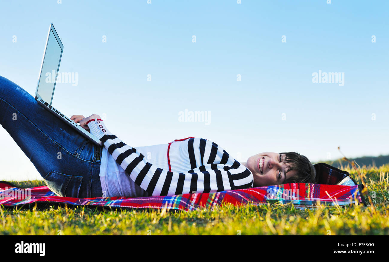 young teen woman work on laptop computer outdoor in nature with blue ...