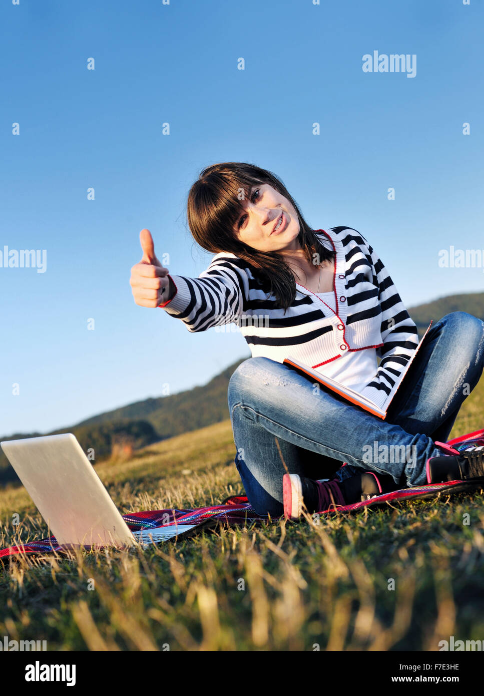young teen woman work on laptop computer outdoor in nature with blue ...