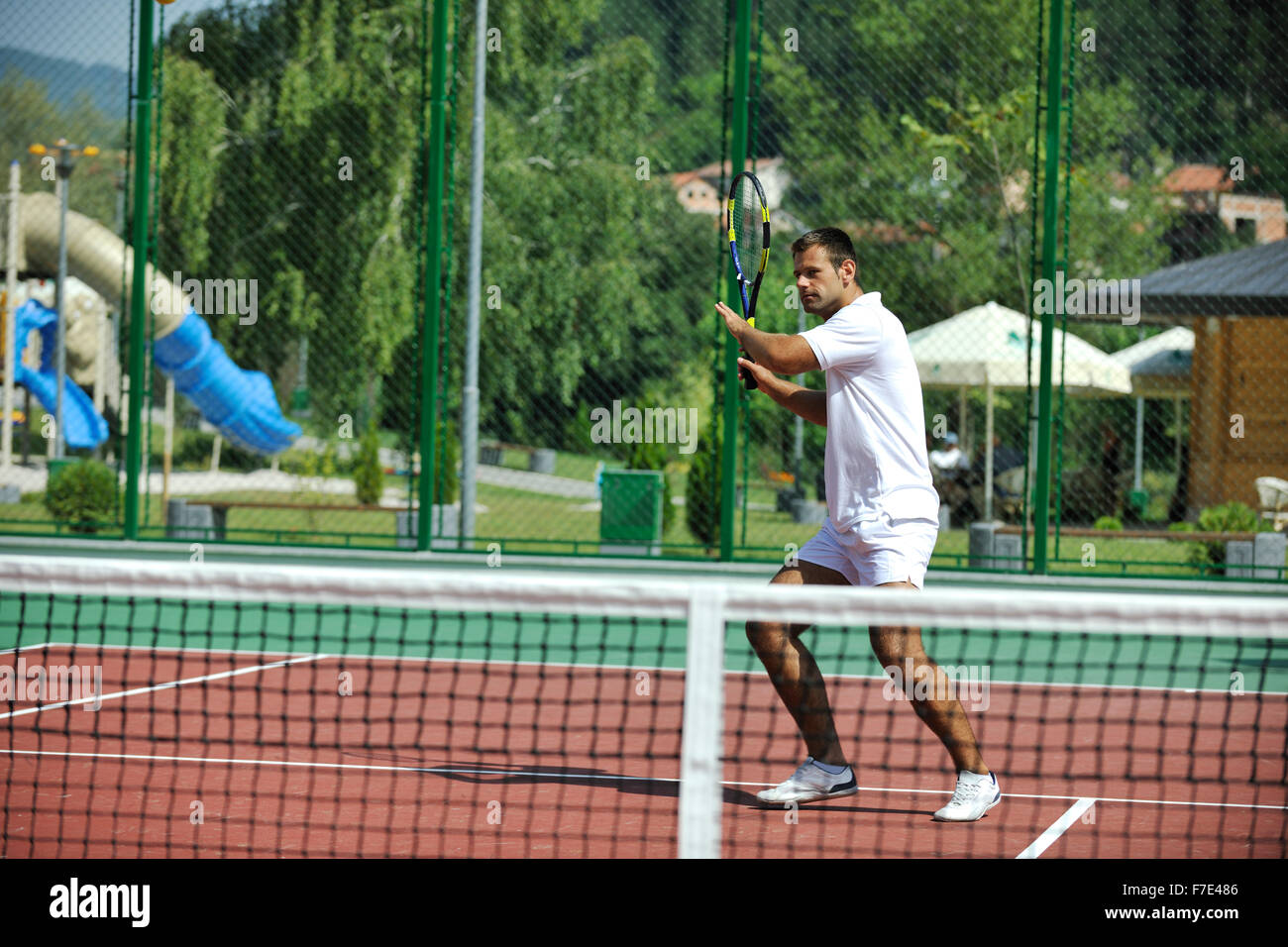 young man play tennis outdoor on orange tennis court at early morning ...
