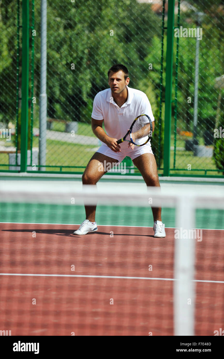 young man play tennis outdoor on orange tennis court at early ...