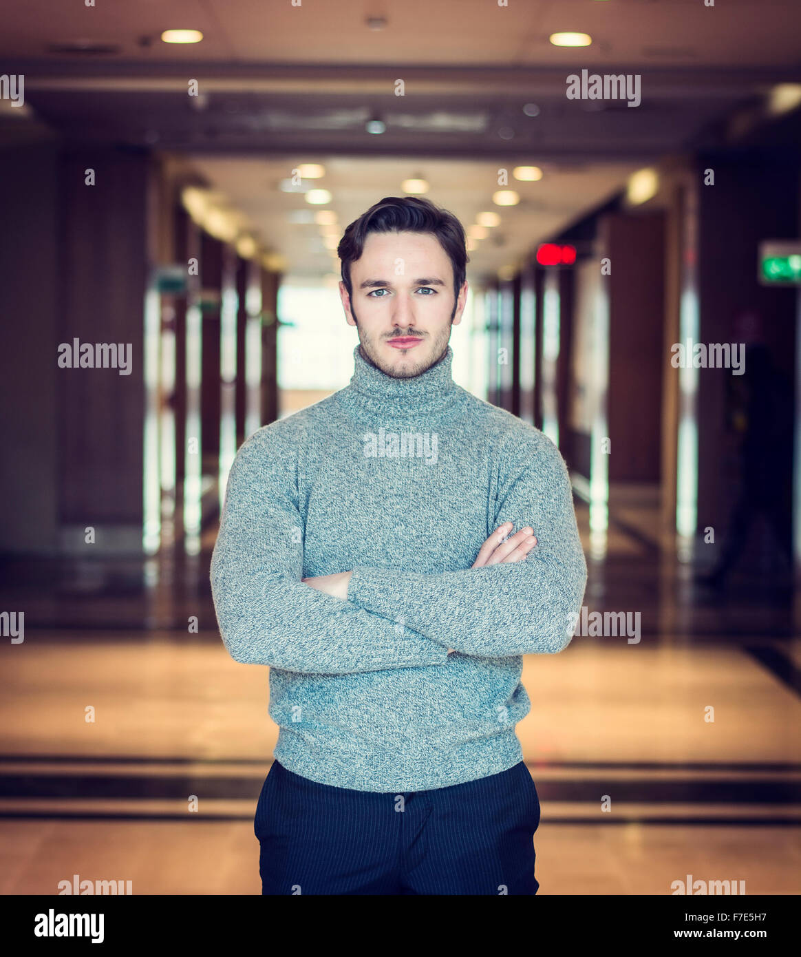 Handsome serious man standing inside modern building with arms crossed ...
