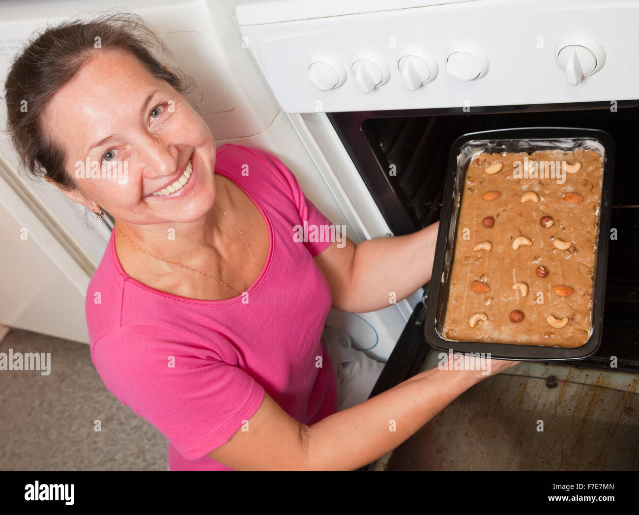 Mature woman putting dough on roasting pan into oven. One of the stages ...