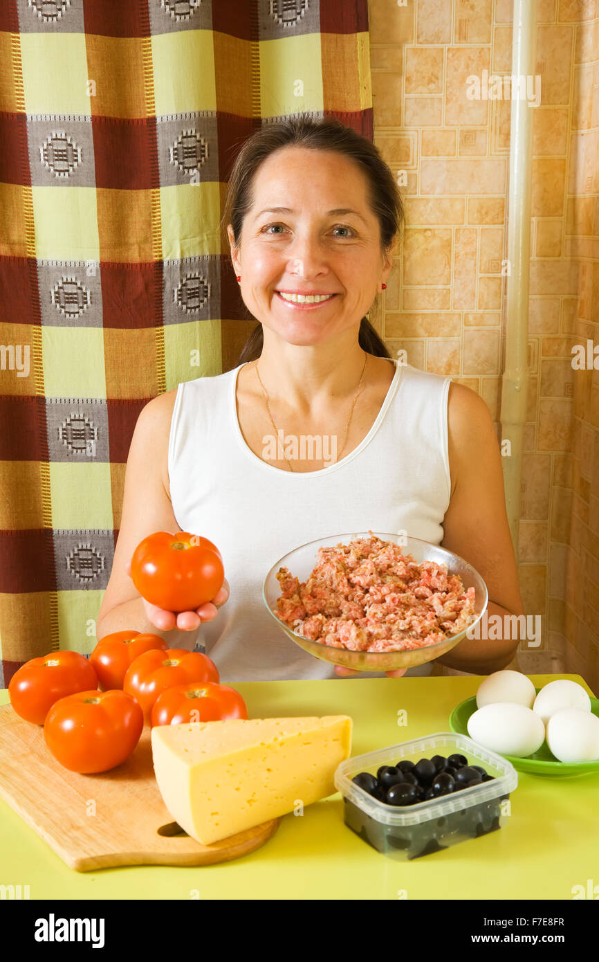 Woman with food products for farci tomato in her kitchen. See in series ...