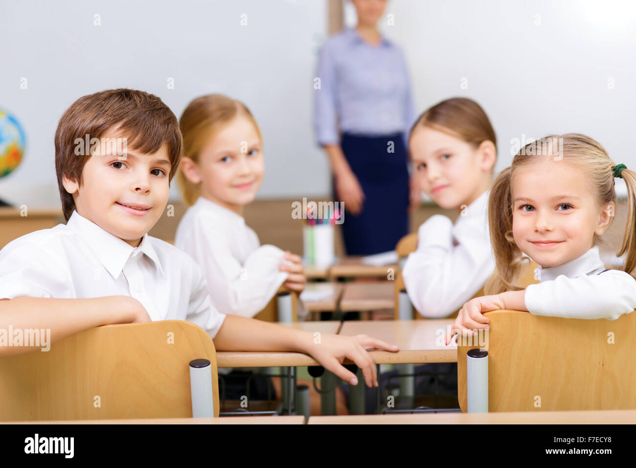 Four smiling pupils sitting at the desk Stock Photo - Alamy