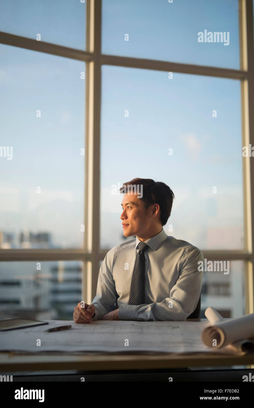Singapore, Architect with building plans looking out window Stock Photo ...