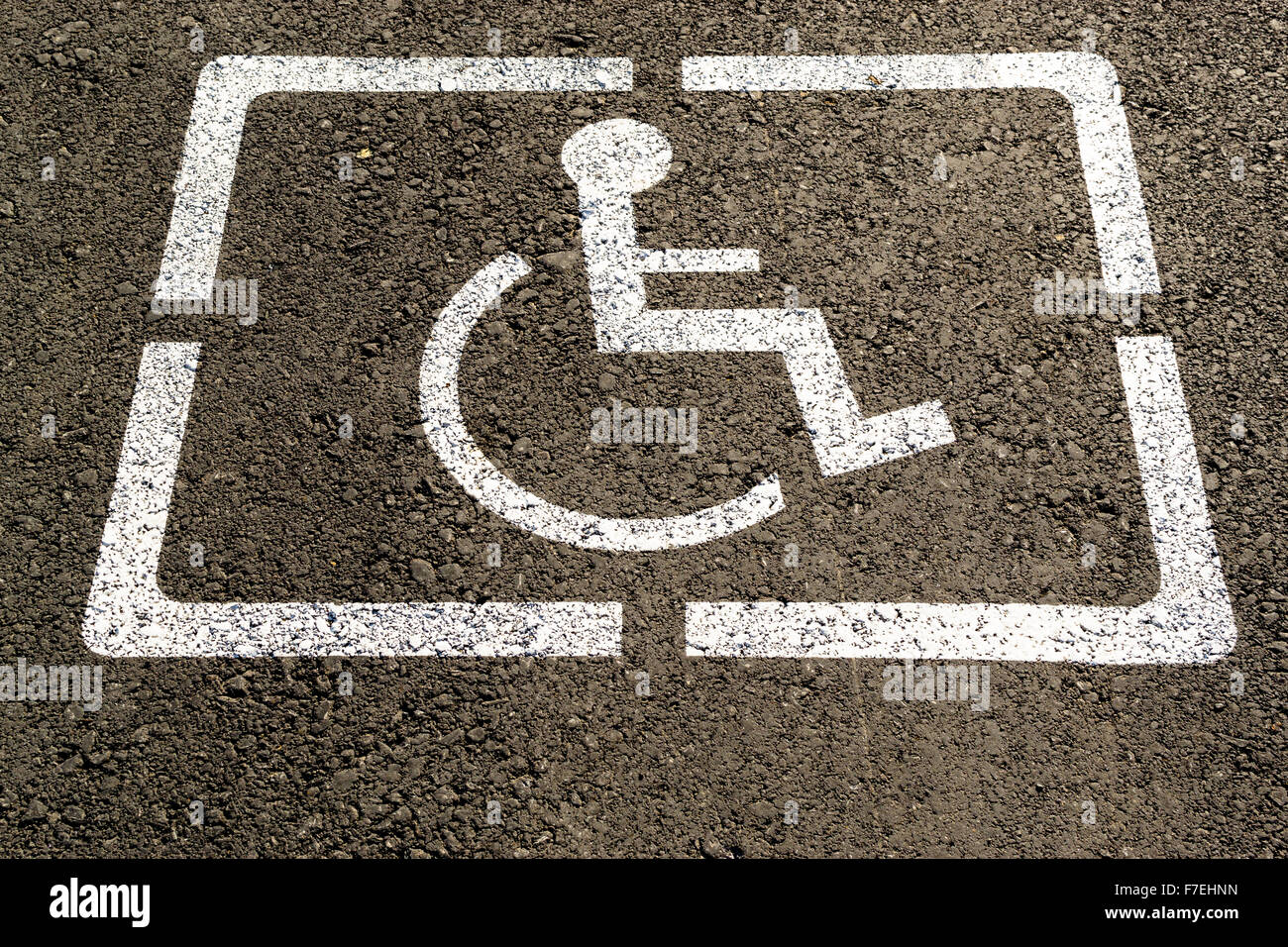 White painted disabled parking space sign on grey asphalt road with ...