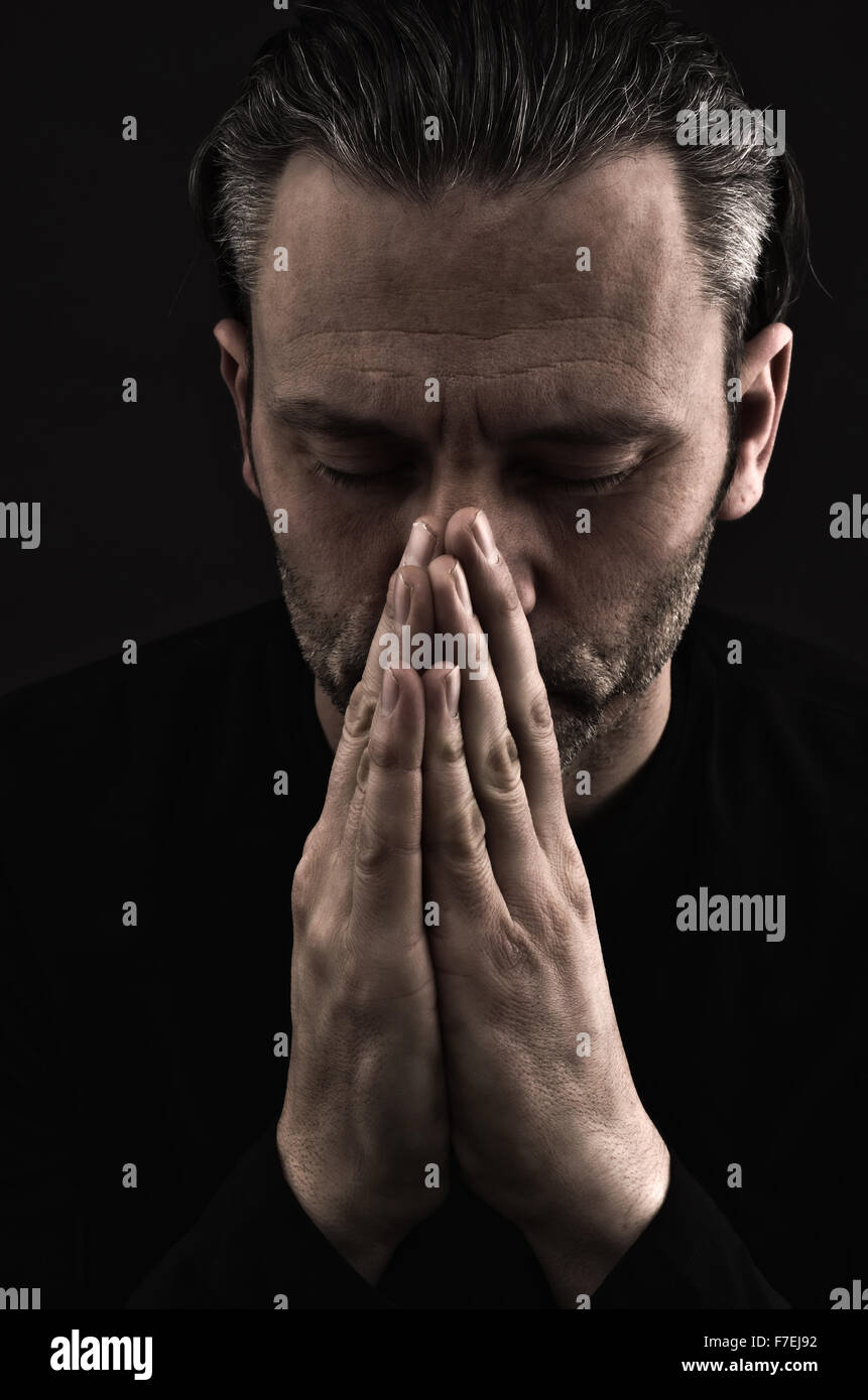 Portrait of sad man praying on a dark background Stock Photo - Alamy