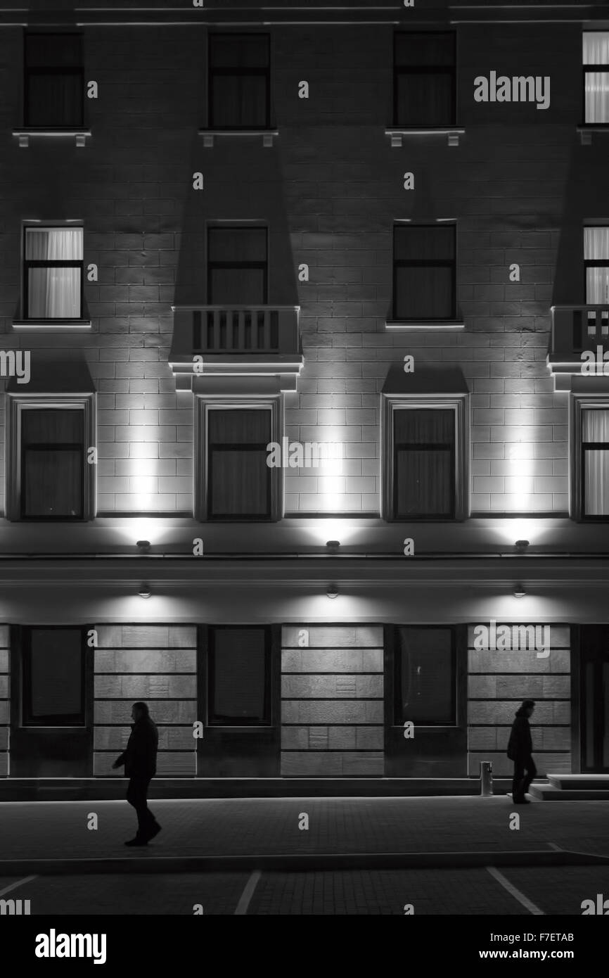 Two people walk in opposite directions against an illuminated building ...