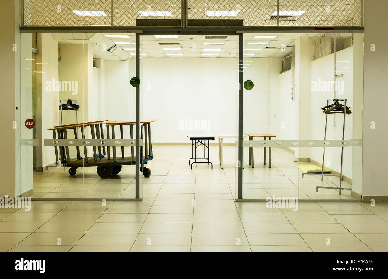 Brightly lit empty shop unit with discarded furniture and strip lights ...