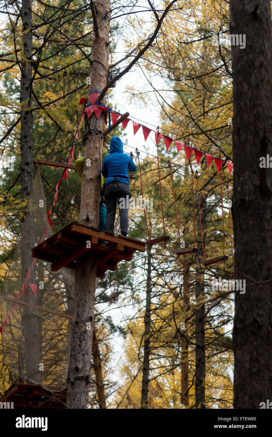 Two young women in safety gear climb trees during an outdoor activity ...
