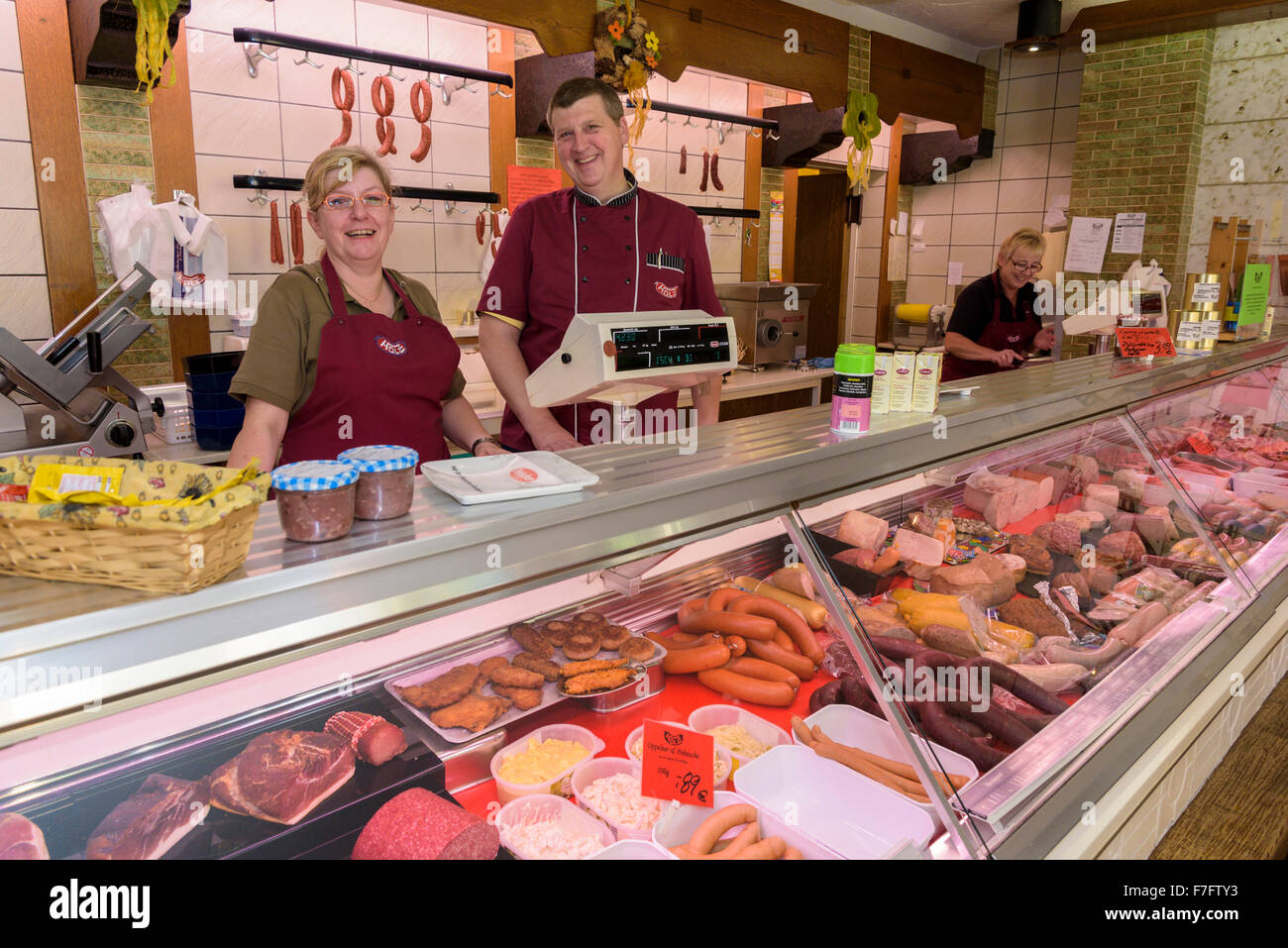 A butcher, his wife, and an employee stand behind the counter in a ...