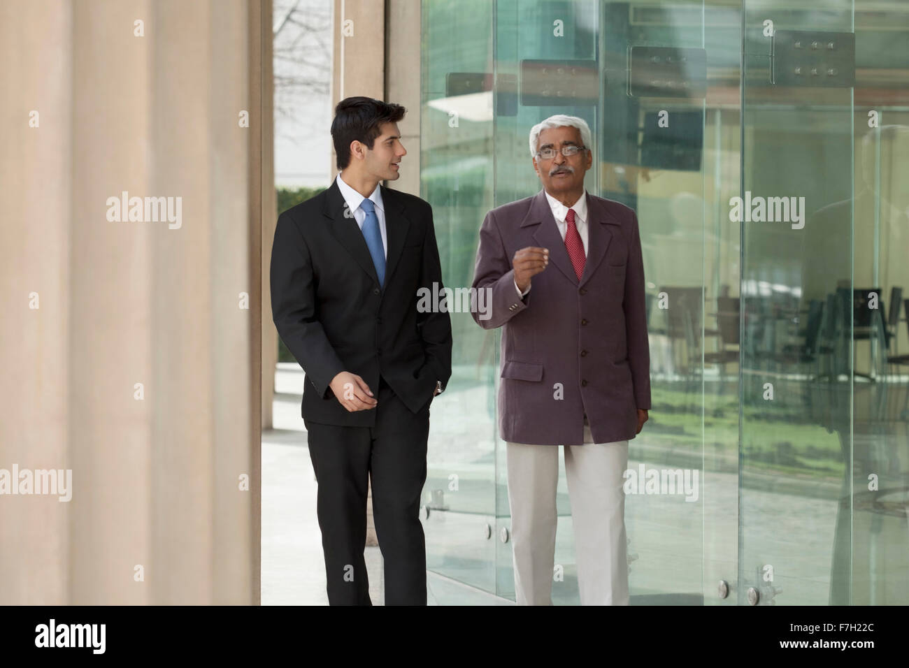 India, Senior and junior businessmen talking outside office building ...