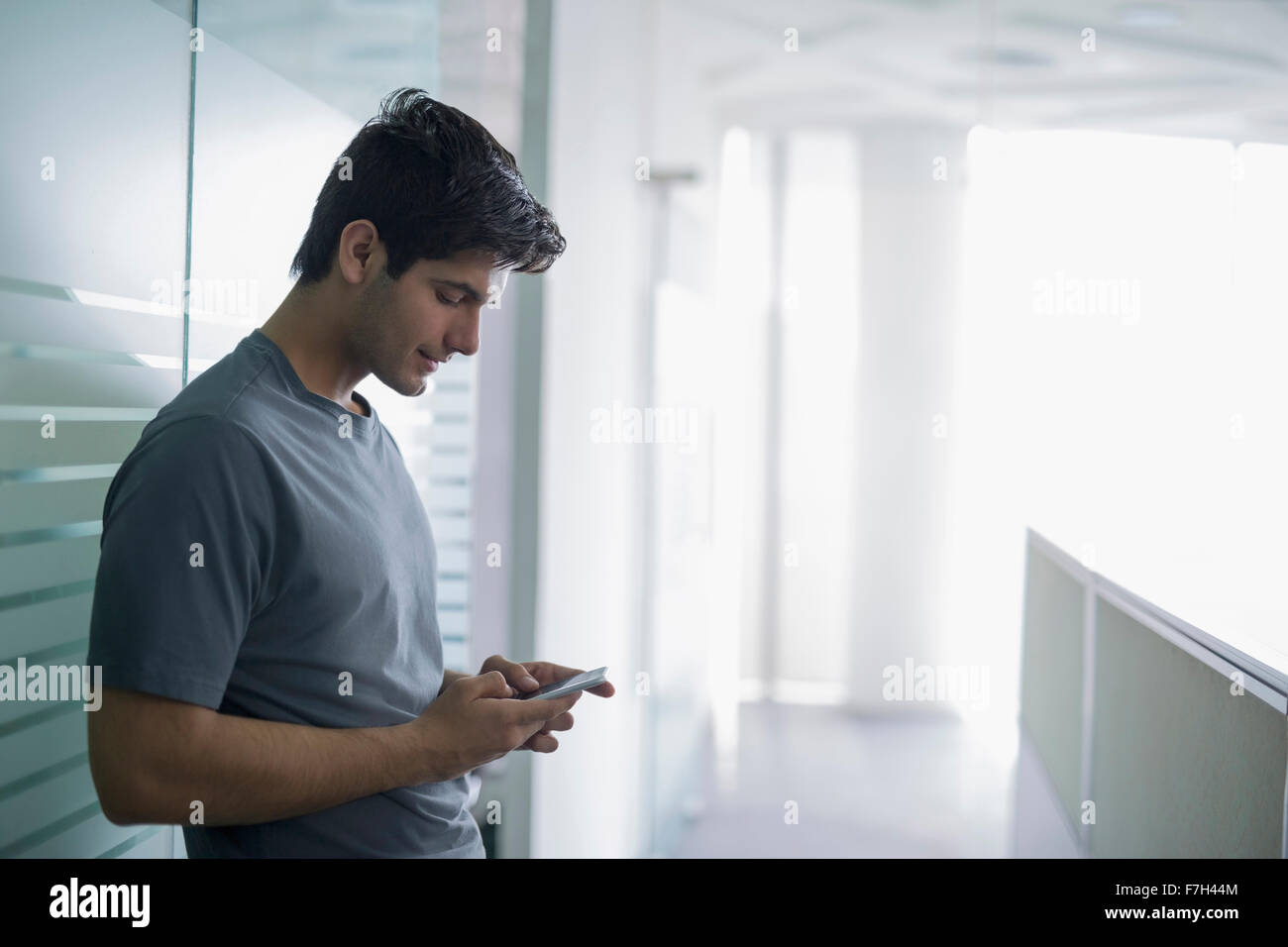 Young man in office looking down at mobile phone Stock Photo - Alamy