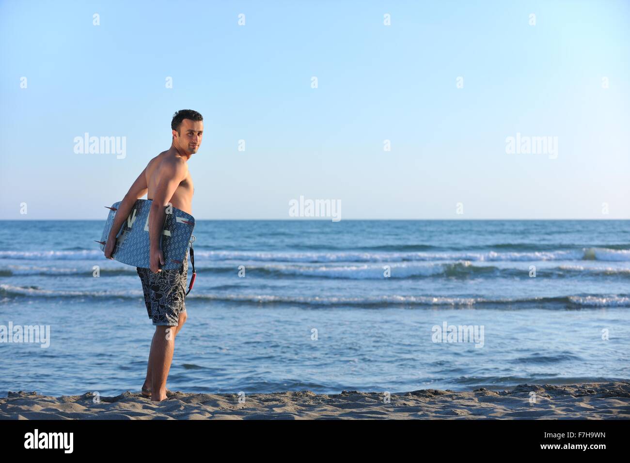 Portrait of a strong young surf man at beach on sunset in a ...