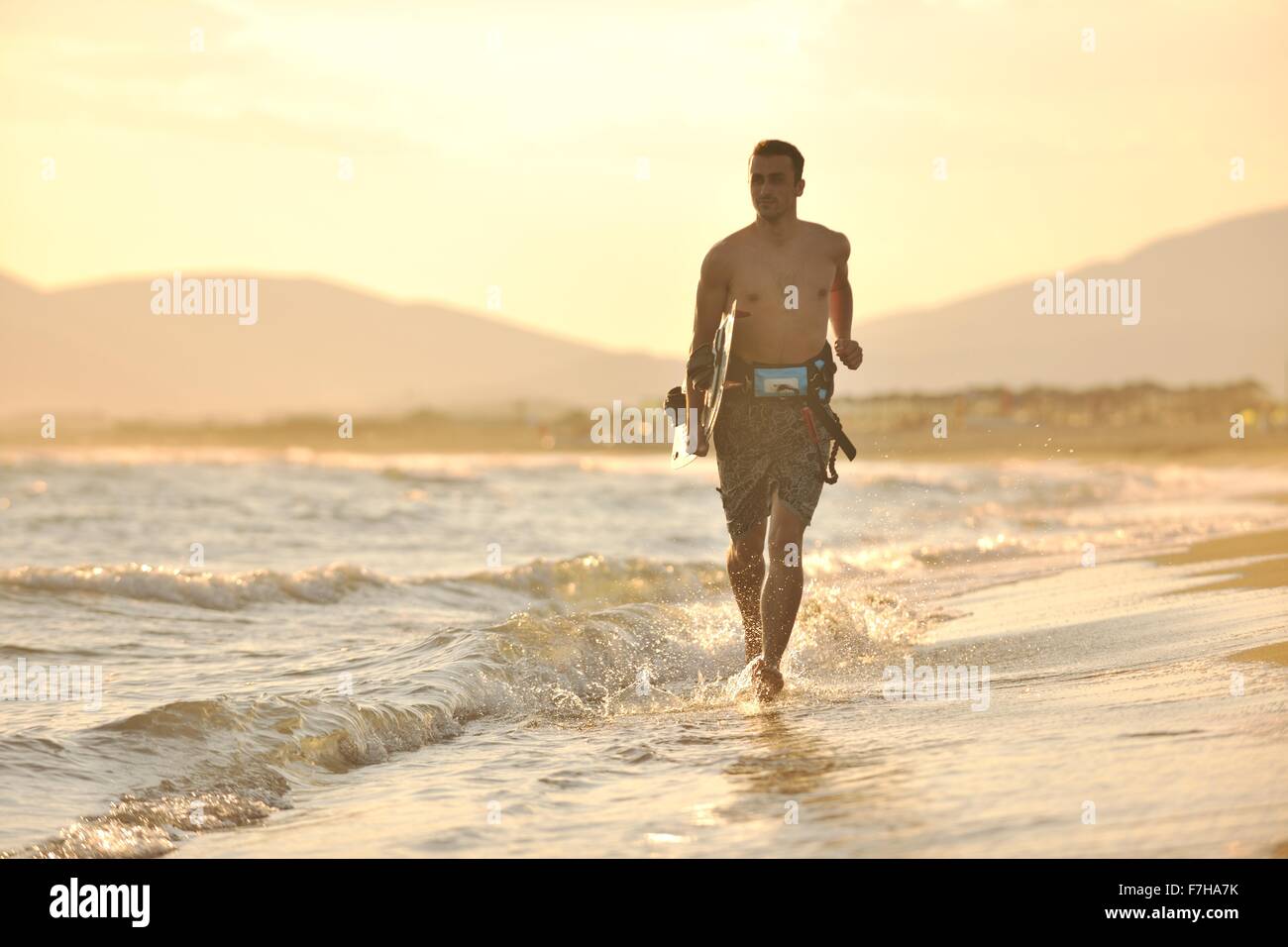 Portrait of a strong young surf man at beach on sunset in a ...