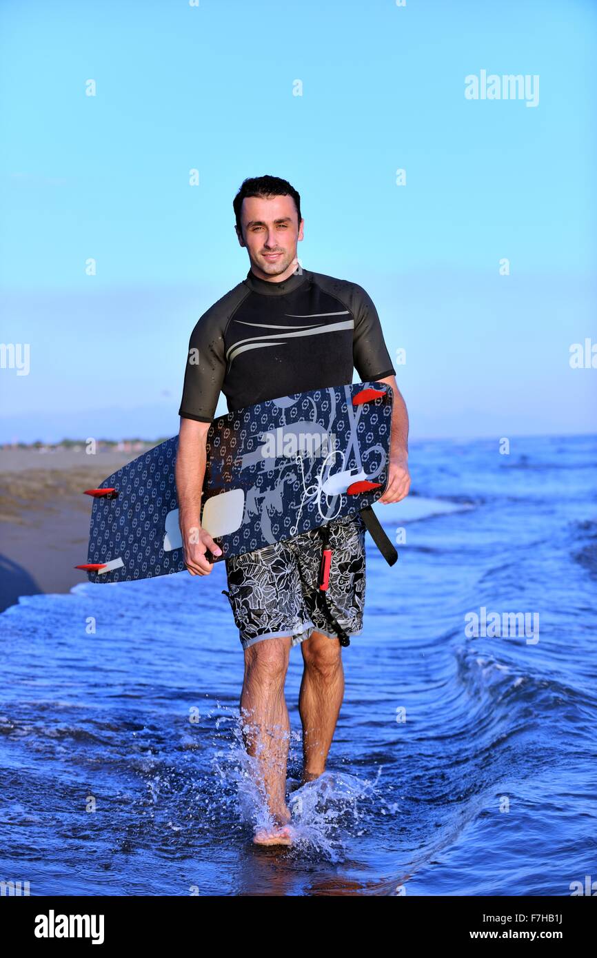 Portrait of a strong young surf man at beach on sunset in a ...