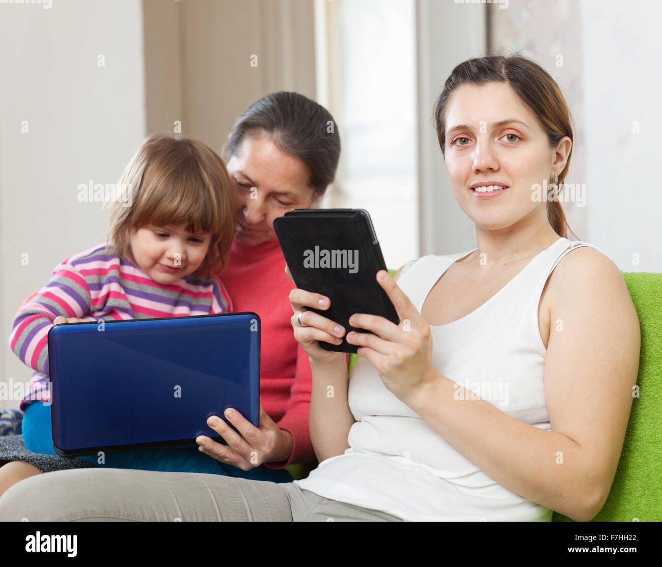 Two women and child using electronic devices on sofa in home Stock ...