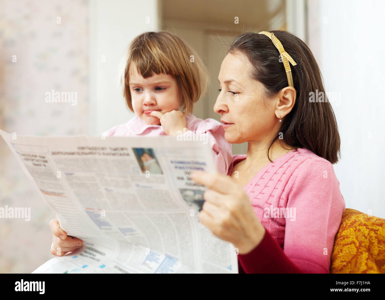 grandmother and child reads newspaper together on couch in home Stock ...