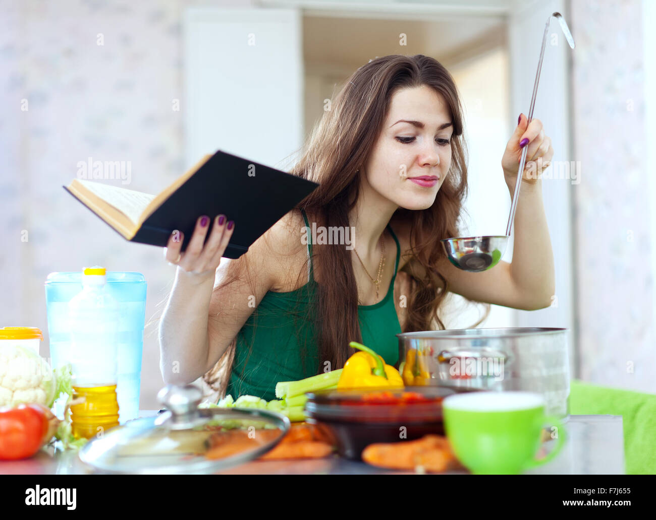 beautiful housewife cooking with ladle and cookbook in kitchen Stock ...