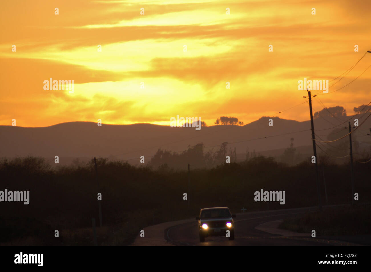Car with headlights on driving round a bend on an empty road, in ...