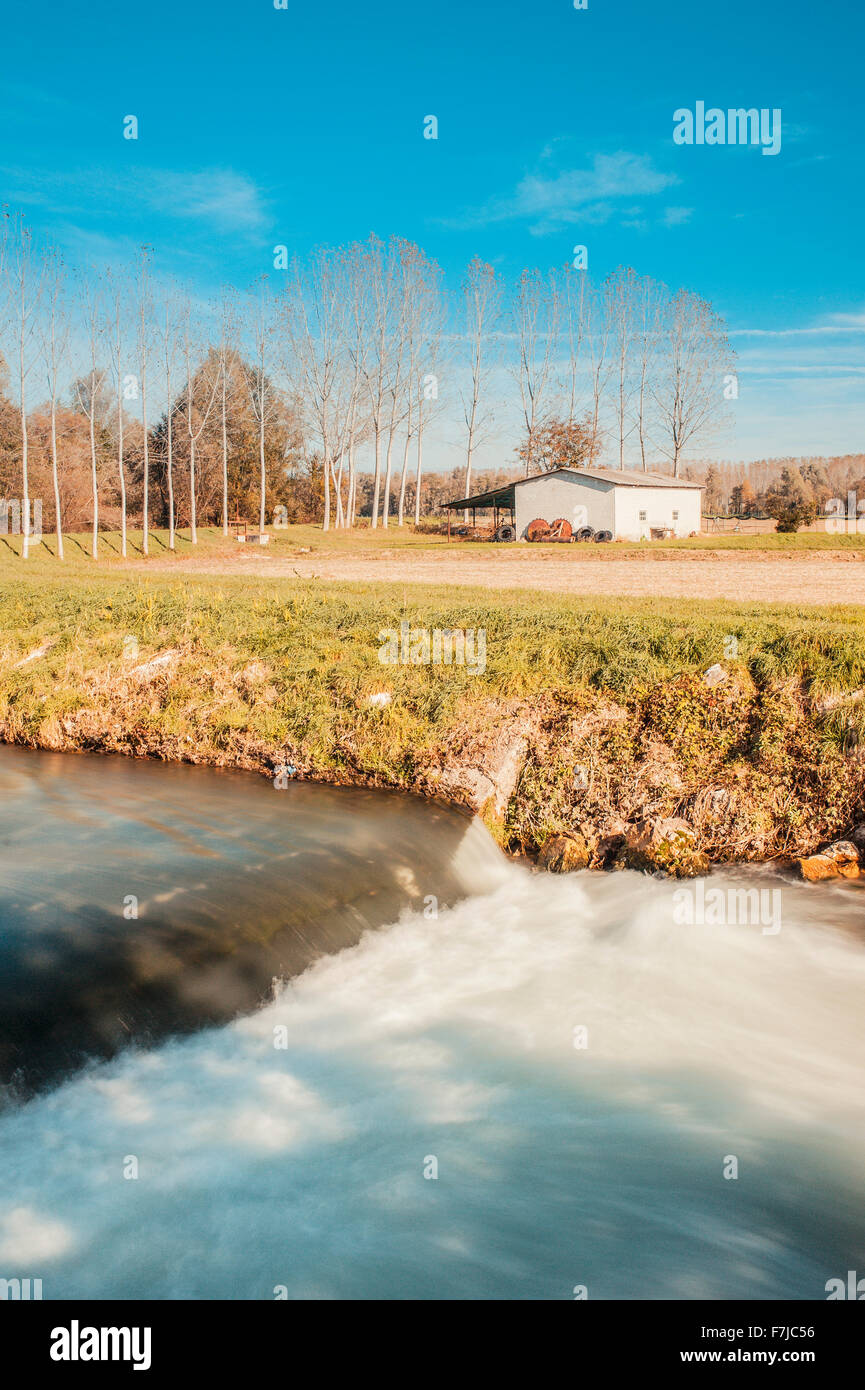Agricultural landscape with a river, waterfall, poplars and an old tool ...
