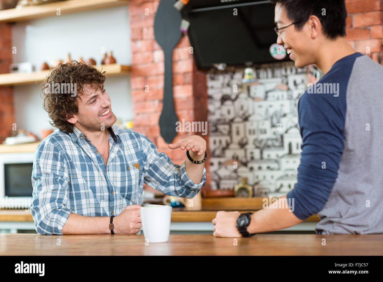 Group of two excited cheerful young guys sitting, talking and laughing ...