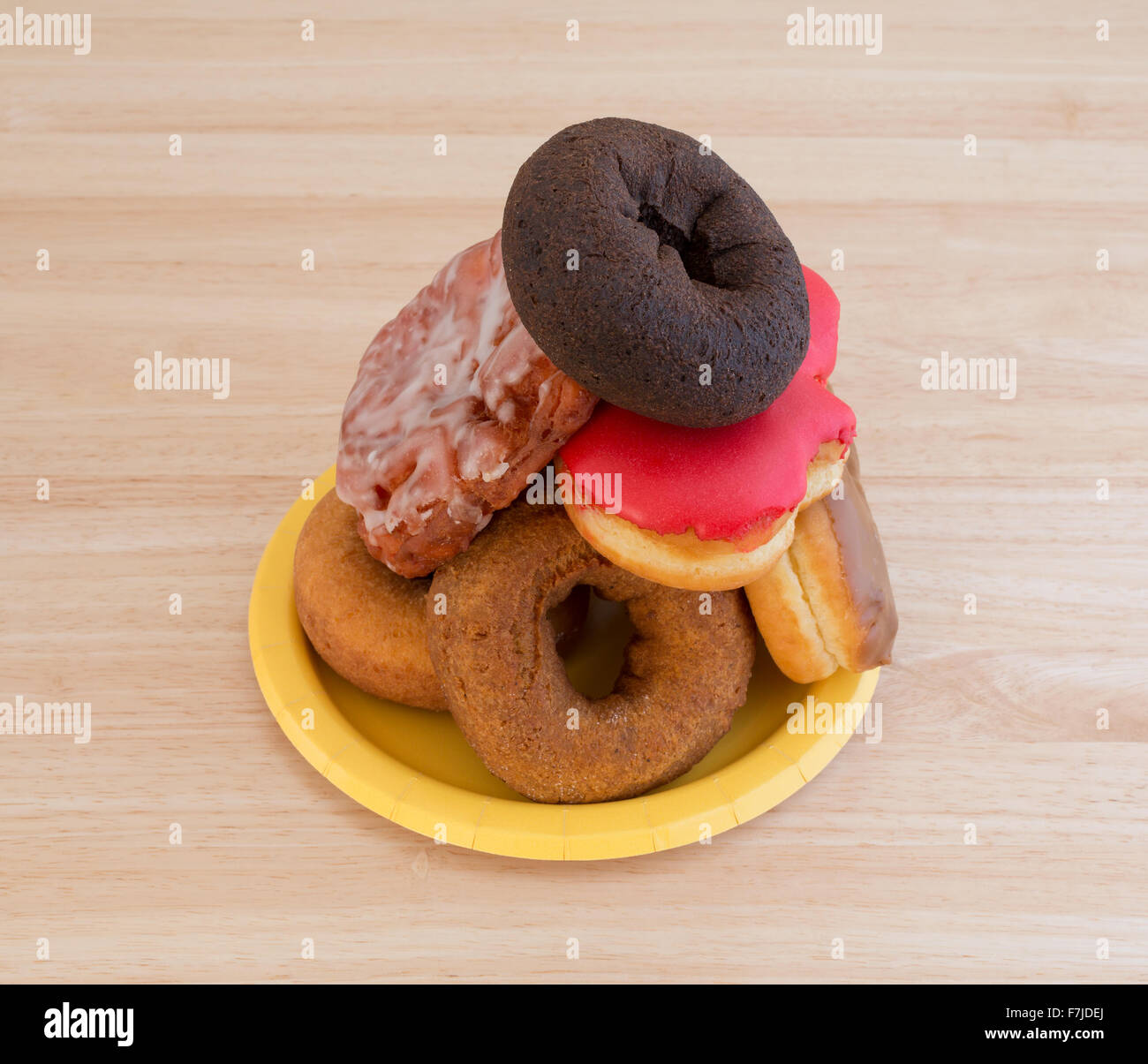 A yellow paper plate with a stack of assorted donuts and iced cherry ...