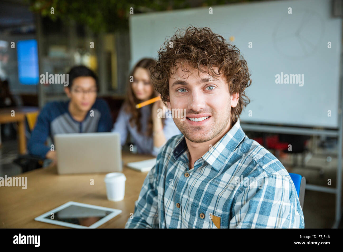 Handsome positive young curly man in plaid shirt sitting and studying ...