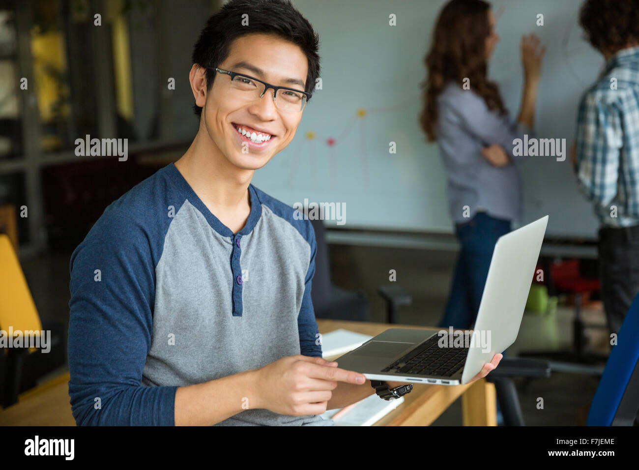 Happy smiling young asian man in glasses holding laptop and studying ...