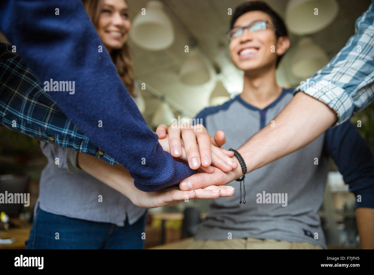 Happy confident young colleagues put hands on top of each other in the ...