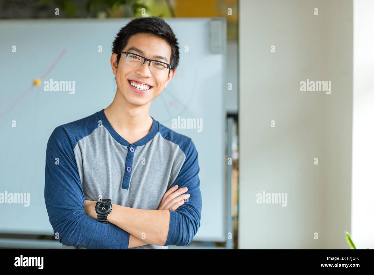 Portrait of a happy asian male student standing with arms folded in ...