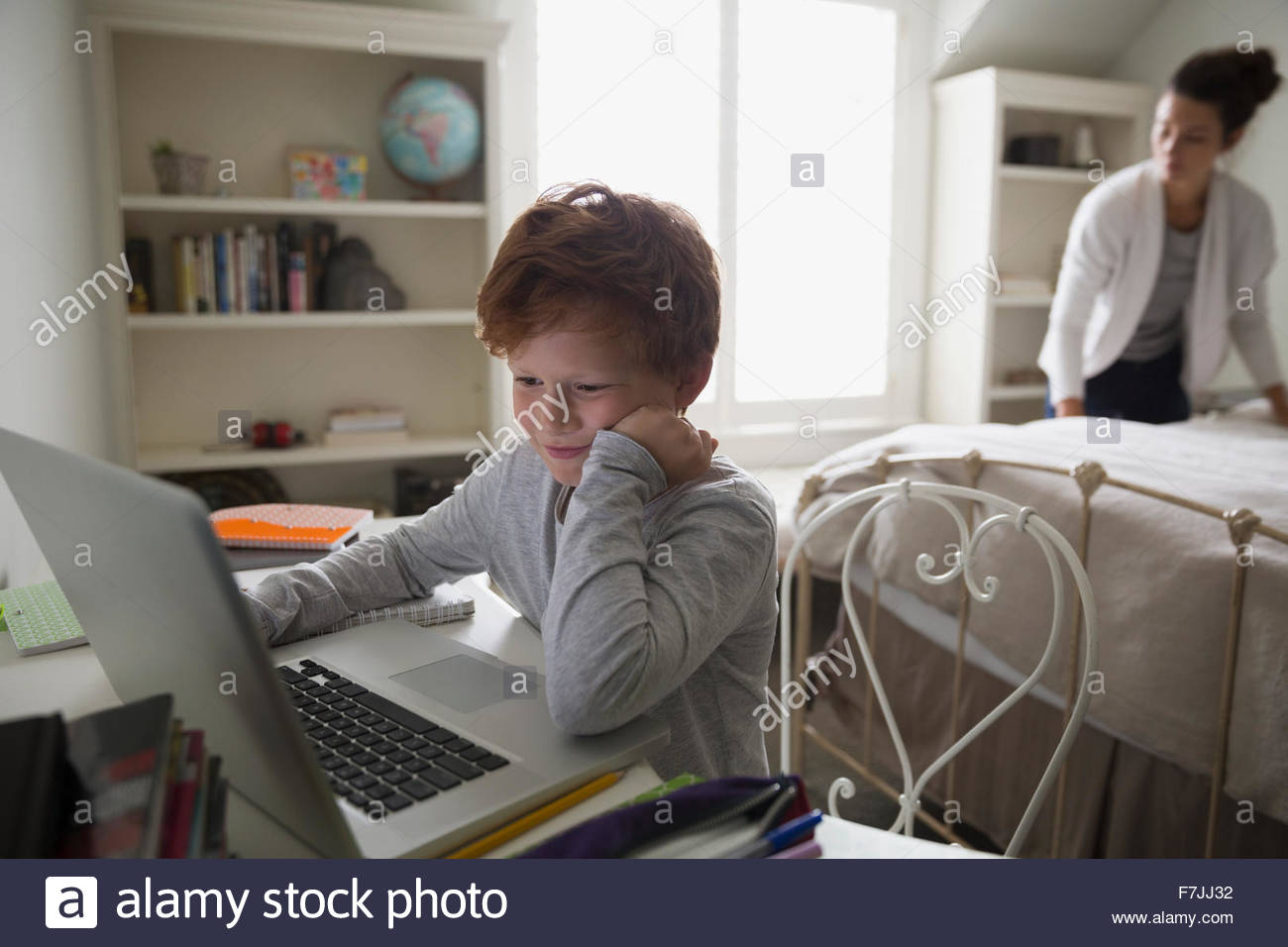 Mother making bed as son does homework laptop Stock Photo - Alamy
