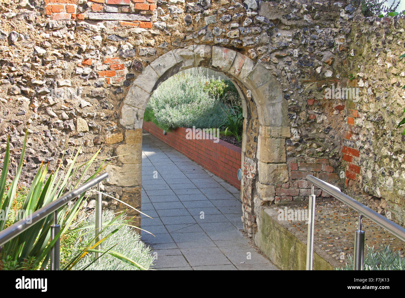 A very ancient flint work and brick archway with a paved path going ...