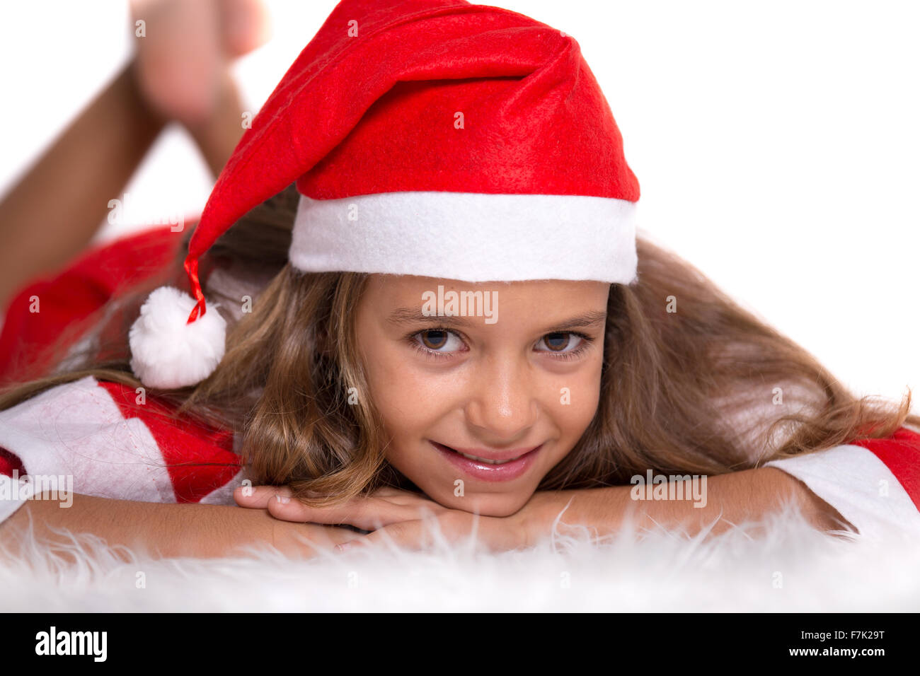 Cute Girl With Christmas Santa Hat And Suit Lying On A Furry White