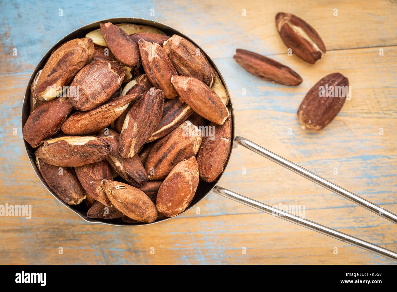 metal measuring scoop of roasted pili nuts against wood background ...
