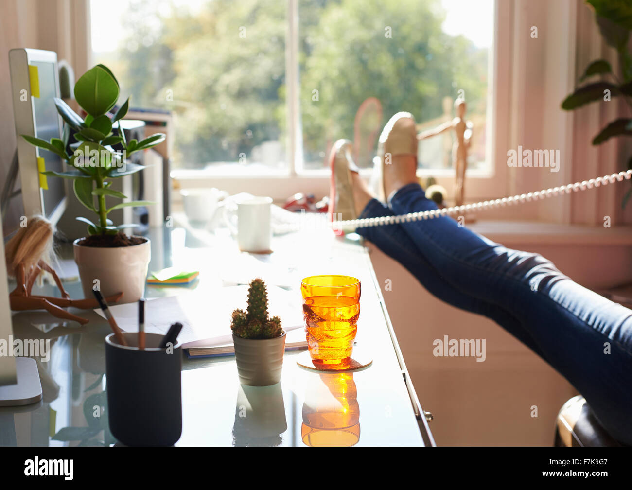 Woman talking on telephone with feet up on desk in sunny home office ...