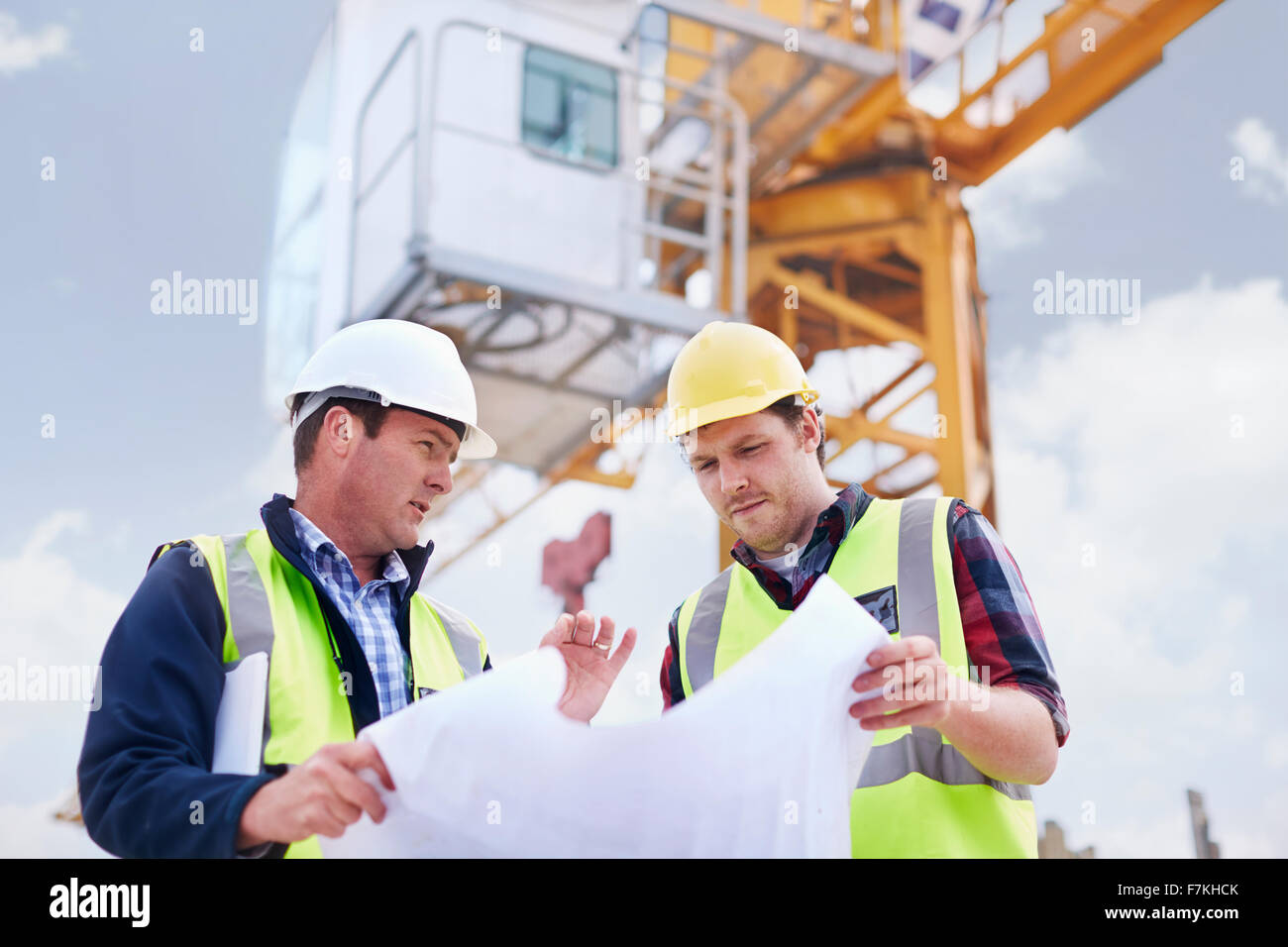 Construction worker and engineer reviewing blueprints below crane at ...
