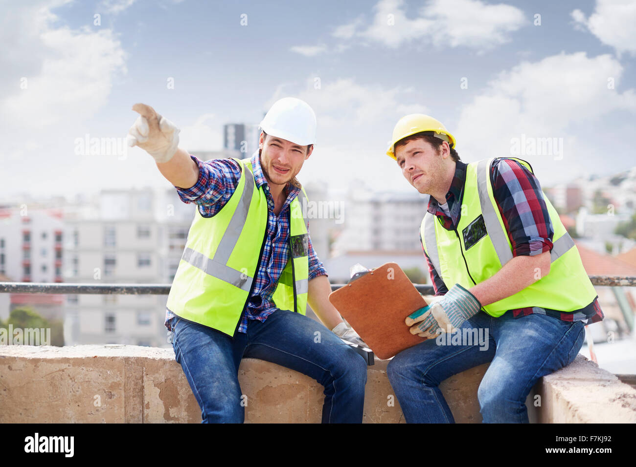 Construction worker and engineer with clipboard pointing at highrise ...