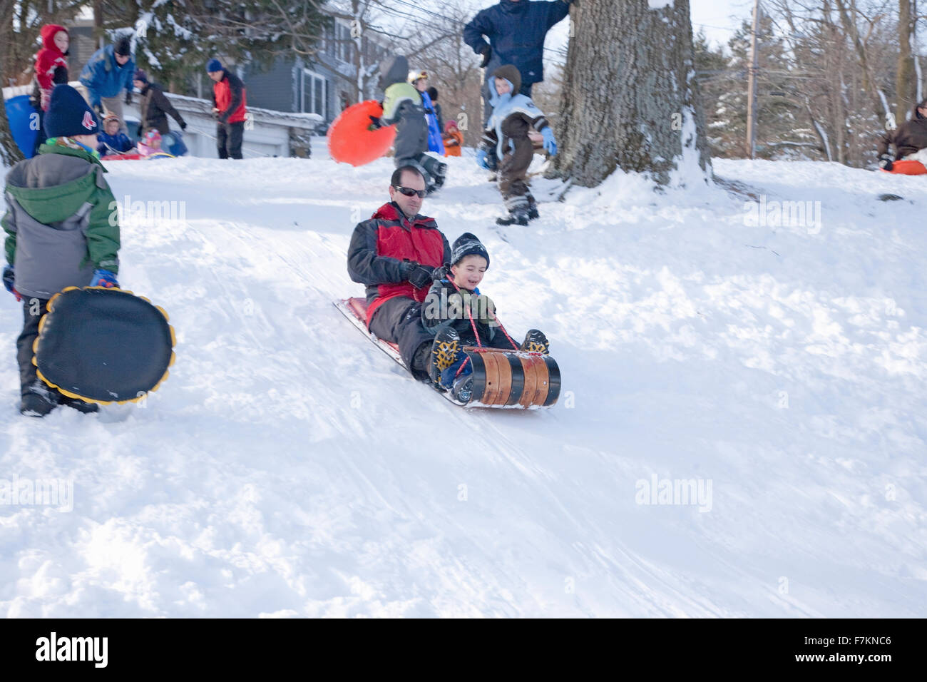 Father and son sleigh ride down in old topogan sled in fresh snow near ...