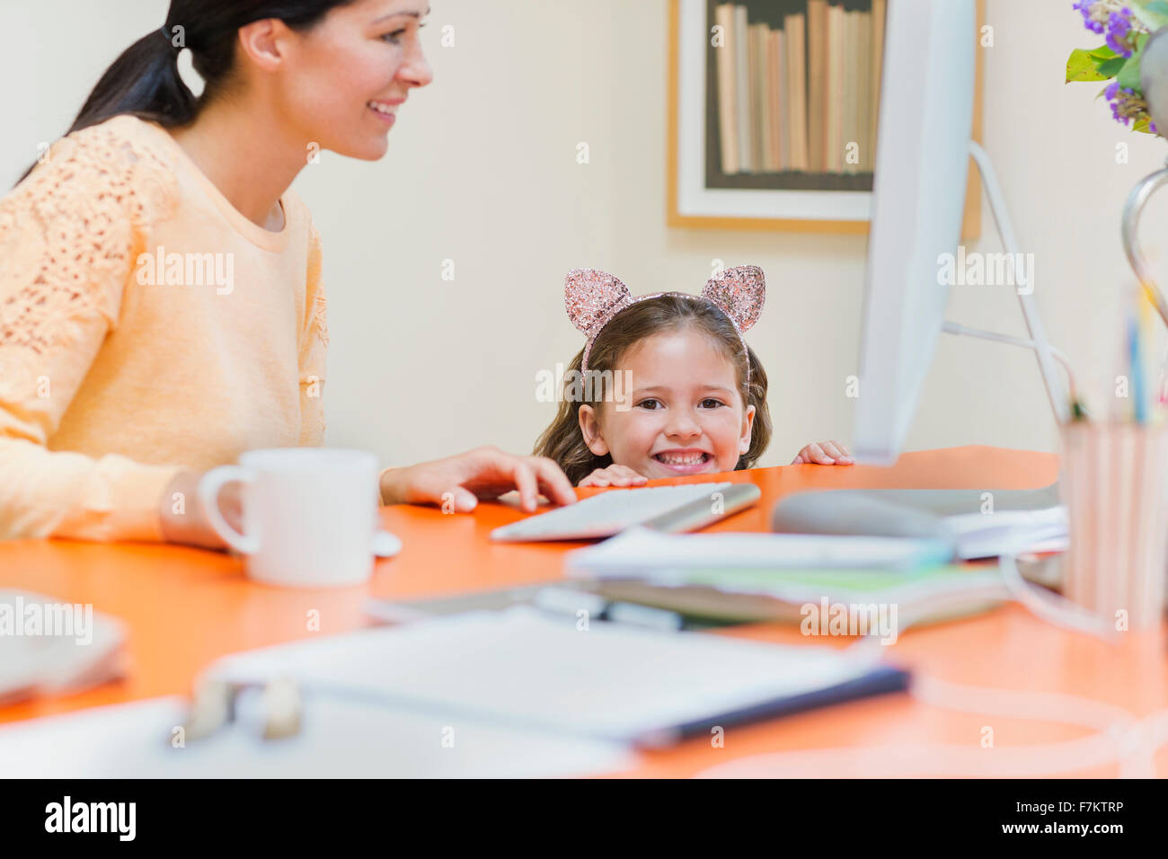 Portrait smiling girl in mouse ears headband with mother at computer ...