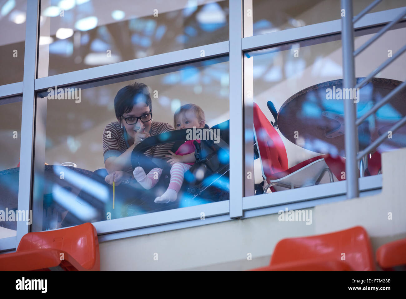baby child in wheels and mom woman looking trough big modern window ...