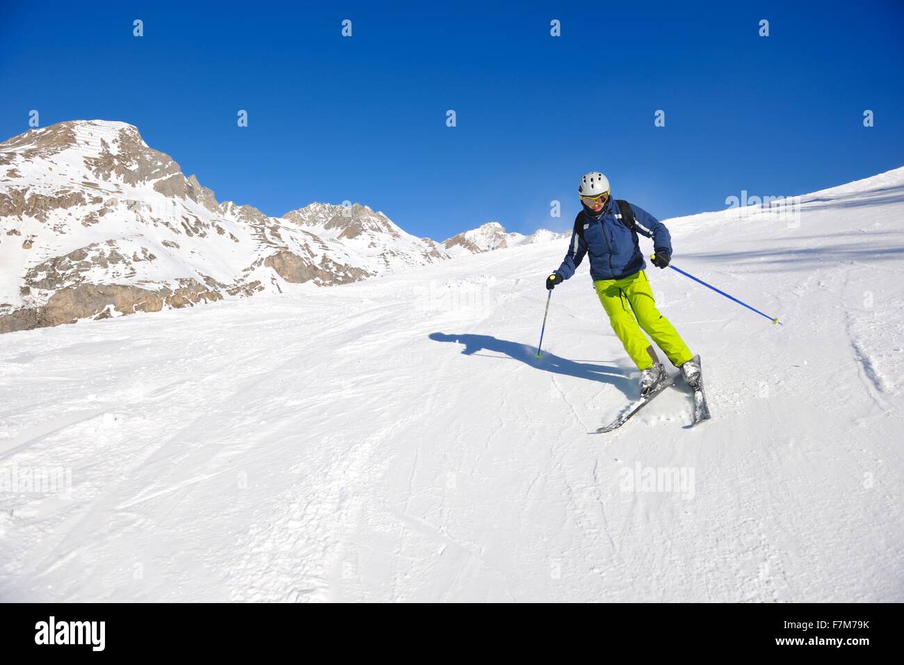 skier skiing downhill on fresh powder snow with sun and mountains in ...