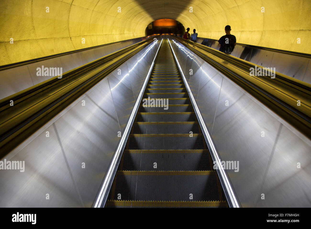 An escalator with passengers moves through oval tube of light to the ...